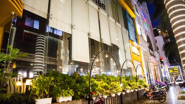 Uma cafeteria com fachada moderna, janelas amplas e uma fileira de vasos com plantas na frente.