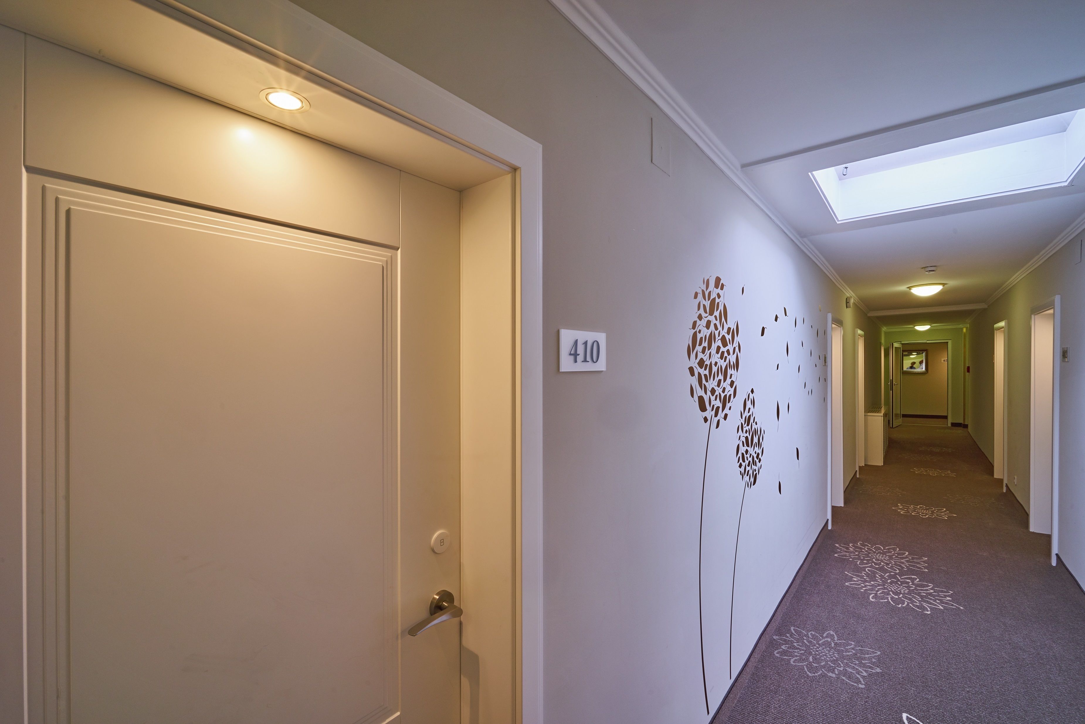 Corredor de hotel com porta fechada, placa de número e design decorativo na parede.