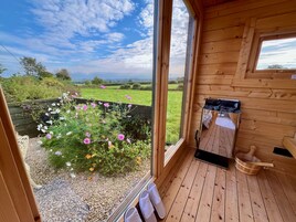 Uma cabana de madeira com uma grande janela que oferece vista para um jardim com flores cor-de-rosa e um céu claro.