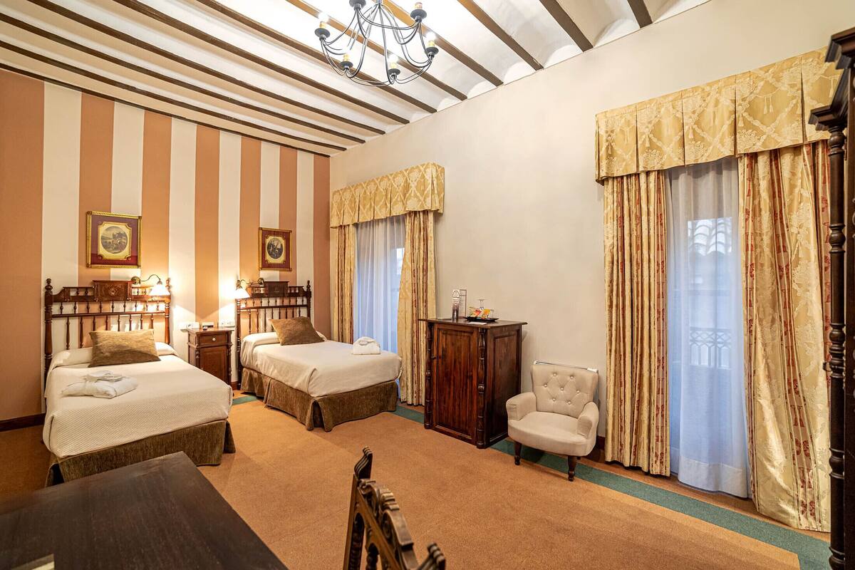 Quarto de hotel com duas camas, um armário de madeira, uma cadeira e um candelabro.