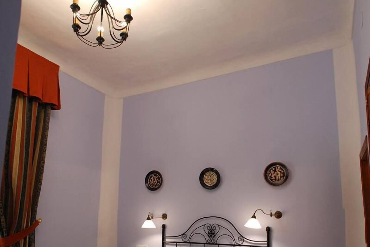 Quarto com cama, duas mesas de cabeceira, um candelabro e detalhes decorativos nas paredes.