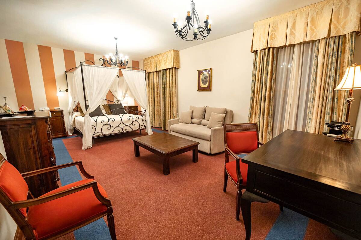 Quarto de hotel com cama de dossel, um sofá, uma mesa de jantar e um piano.