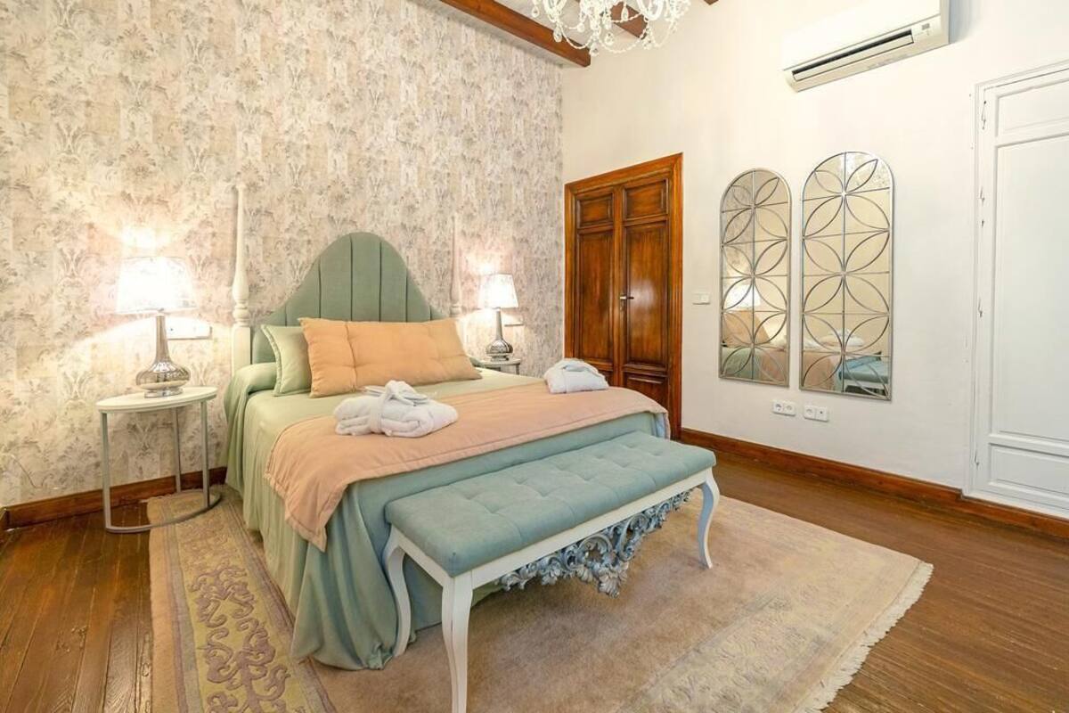 Quarto com cama, abajures, um banquinho, guarda-roupa de madeira e painéis de vidro decorativos.