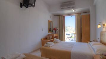 Quarto de hotel com duas camas, uma televisão, uma mesa de trabalho com telefone e uma varanda com vista.