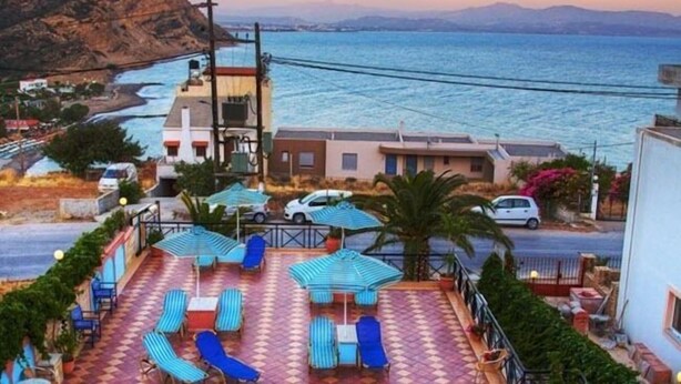 Pátio de hotel à beira-mar com espreguiçadeiras e guarda-sóis, com vista para o mar e uma paisagem montanhosa.