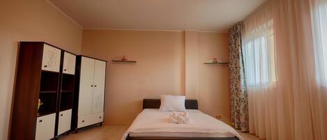 Quarto de hotel com cama, guarda-roupa, mesa de cabeceira e janela com cortinas.