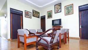 Um quarto com uma cadeira e um sofá de madeira, uma televisão e obras de arte emolduradas nas paredes.
