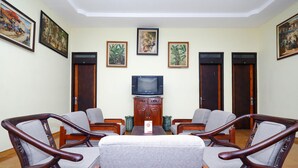 Uma sala de conferências com uma mesa de madeira, quatro cadeiras cinzas, uma televisão e quadros nas paredes.