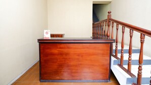 Uma mesa de recepção com acabamento em madeira, piso ladrilhado e escada com balaústres de madeira.