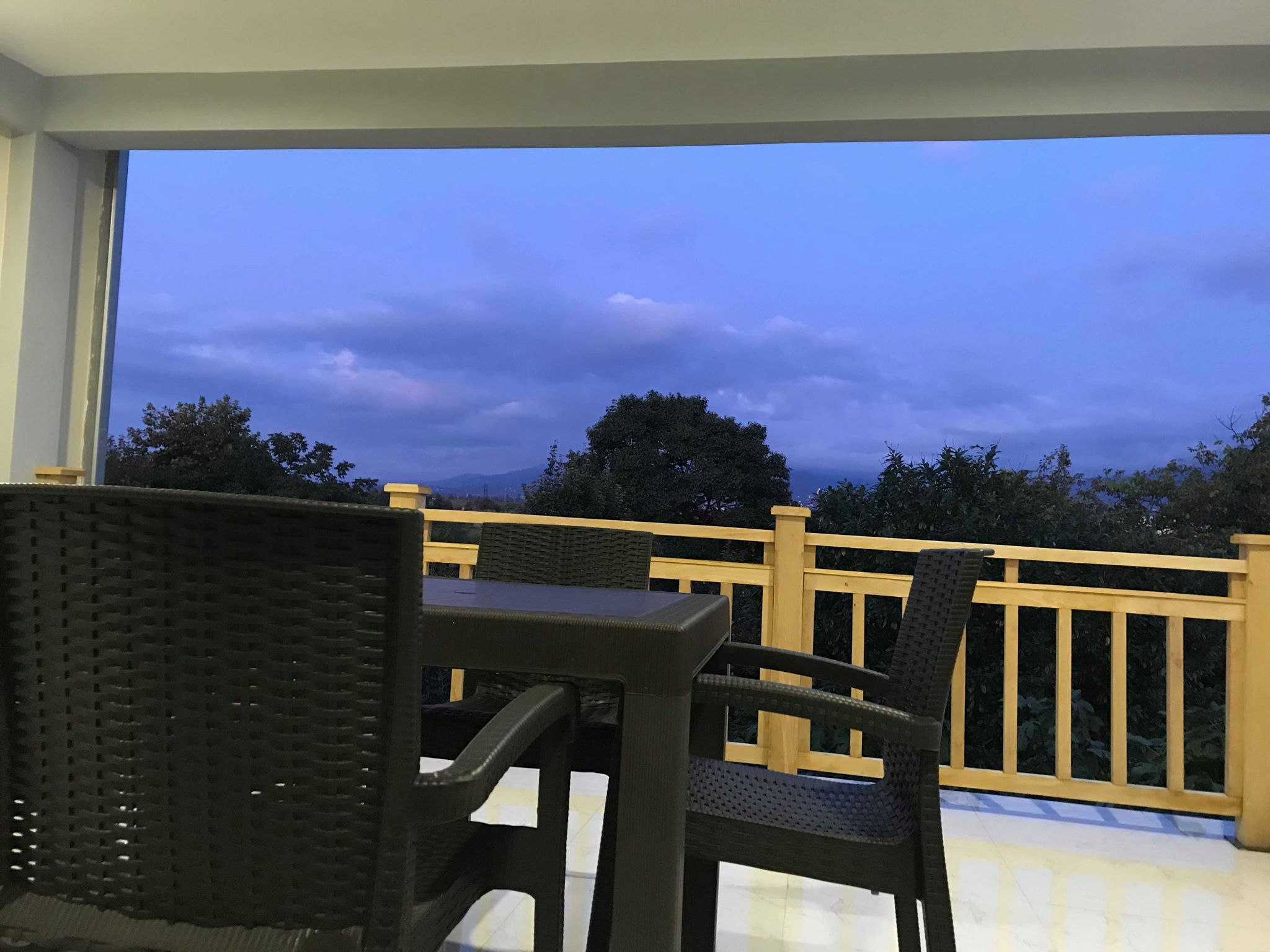Varanda com vista para árvores e montanhas sob um céu nublado.