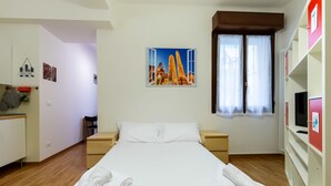 Quarto de hotel com cama, escrivaninha, cadeira, televisão e um quadro na parede.