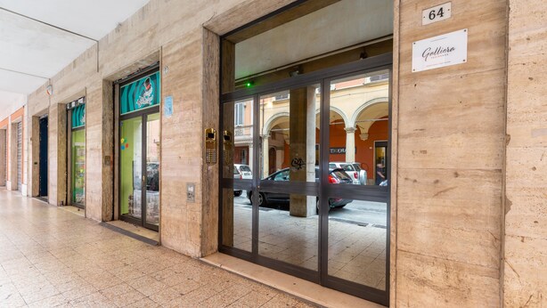 Entrada de hotel com uma grande porta de vidro, uma placa indicando o quarto 64 e vista para a rua.