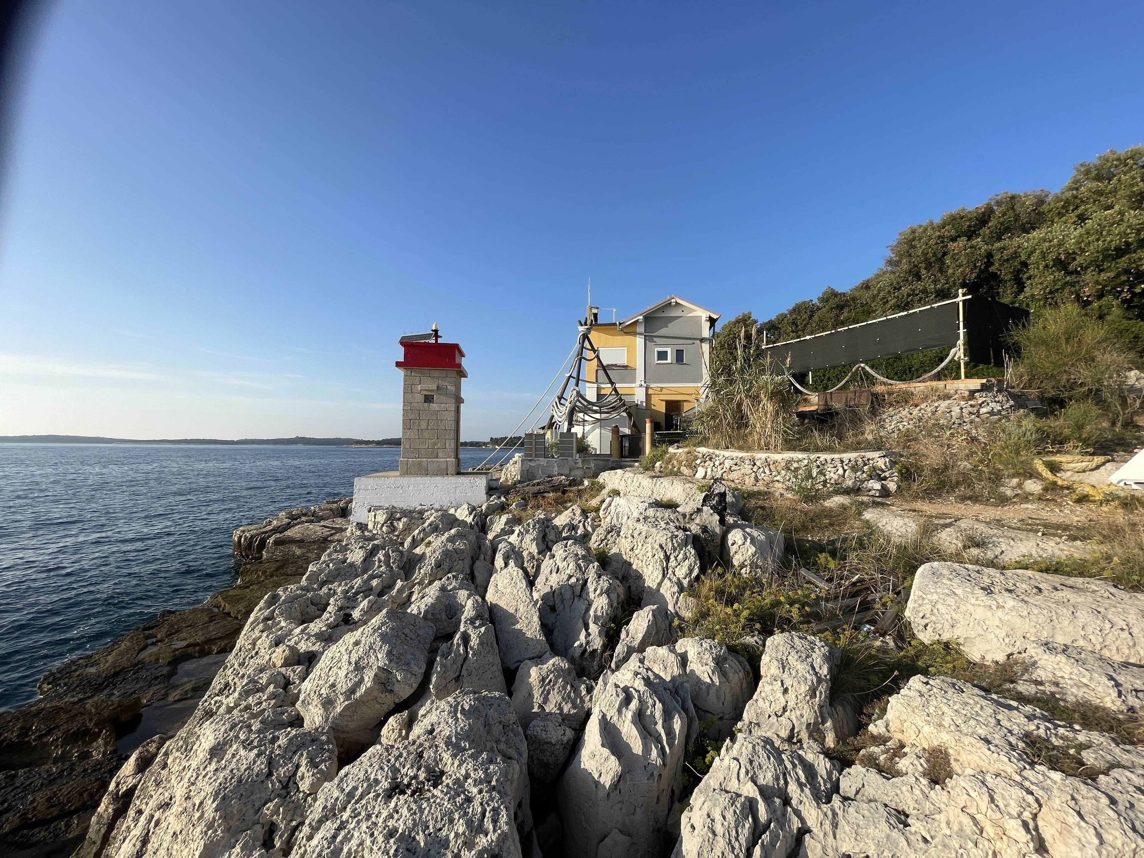 Cena costeira com um farol, terreno rochoso e uma casa com varanda com vista para o mar.