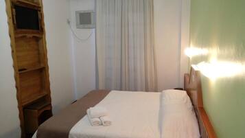 Quarto de hotel com cama, guarda-roupa de madeira, janela com cortinas e luminária na parede.