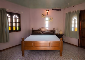 Quarto com cama de madeira, mesa de cabeceira, luminária na parede e janela com cortinas.
