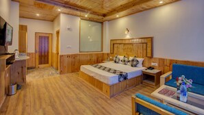 Quarto com painéis de madeira, uma cama, mesa de cabeceira e um pequeno espaço de estar com mesa e flores.
