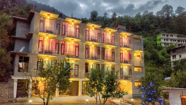 Um hotel com vários andares, varandas, fachada de pedra e uma escadaria que leva à entrada.