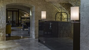 Interior com paredes de pedra, uma mesa de recepção, área de estar e vista para outro espaço.