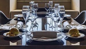 Mesa de jantar posta para refeição, com vista para palmeiras e edifícios através de uma grande janela.