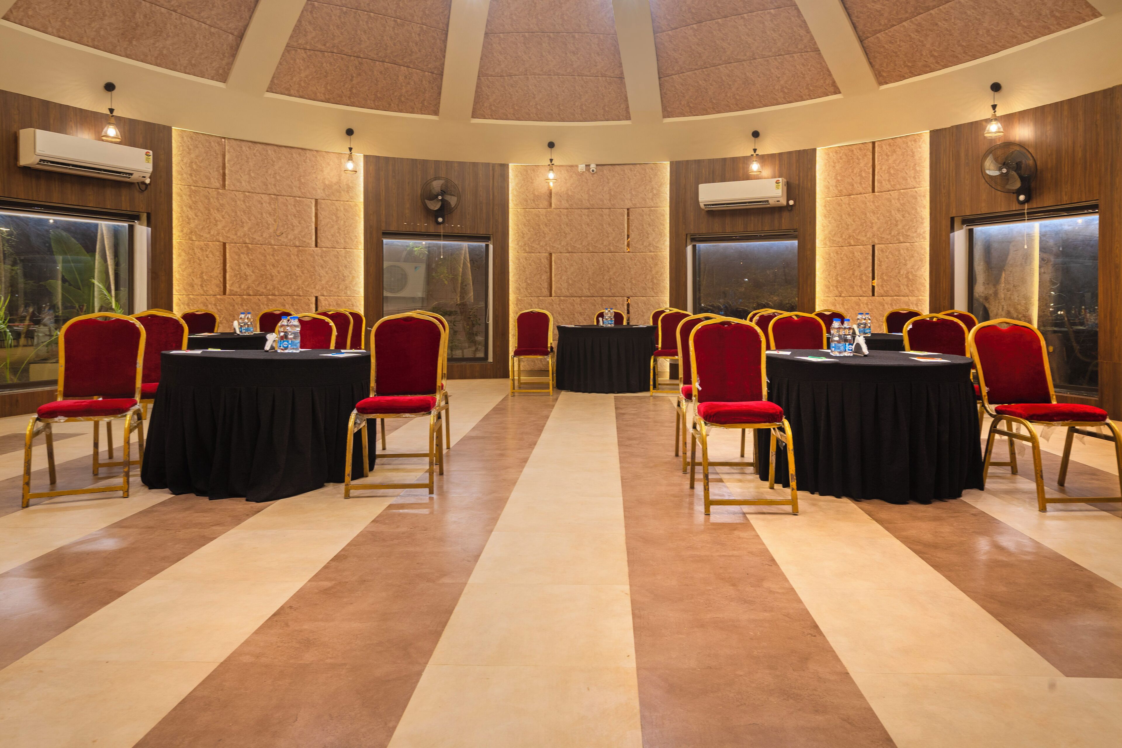 Uma sala de conferências com pé direito alto, várias mesas e cadeiras, e grandes janelas.