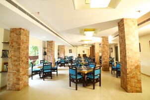 Uma sala de jantar ampla com várias mesas e cadeiras, pilares de pedra e teto iluminado com focos.