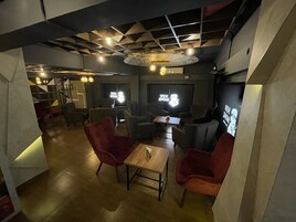 Uma área de lounge moderna com design geométrico no teto, assentos confortáveis e uma mesa central.