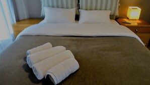 Uma cama bem arrumada com lençóis brancos, um abajur e toalhas dobradas sobre a cama.