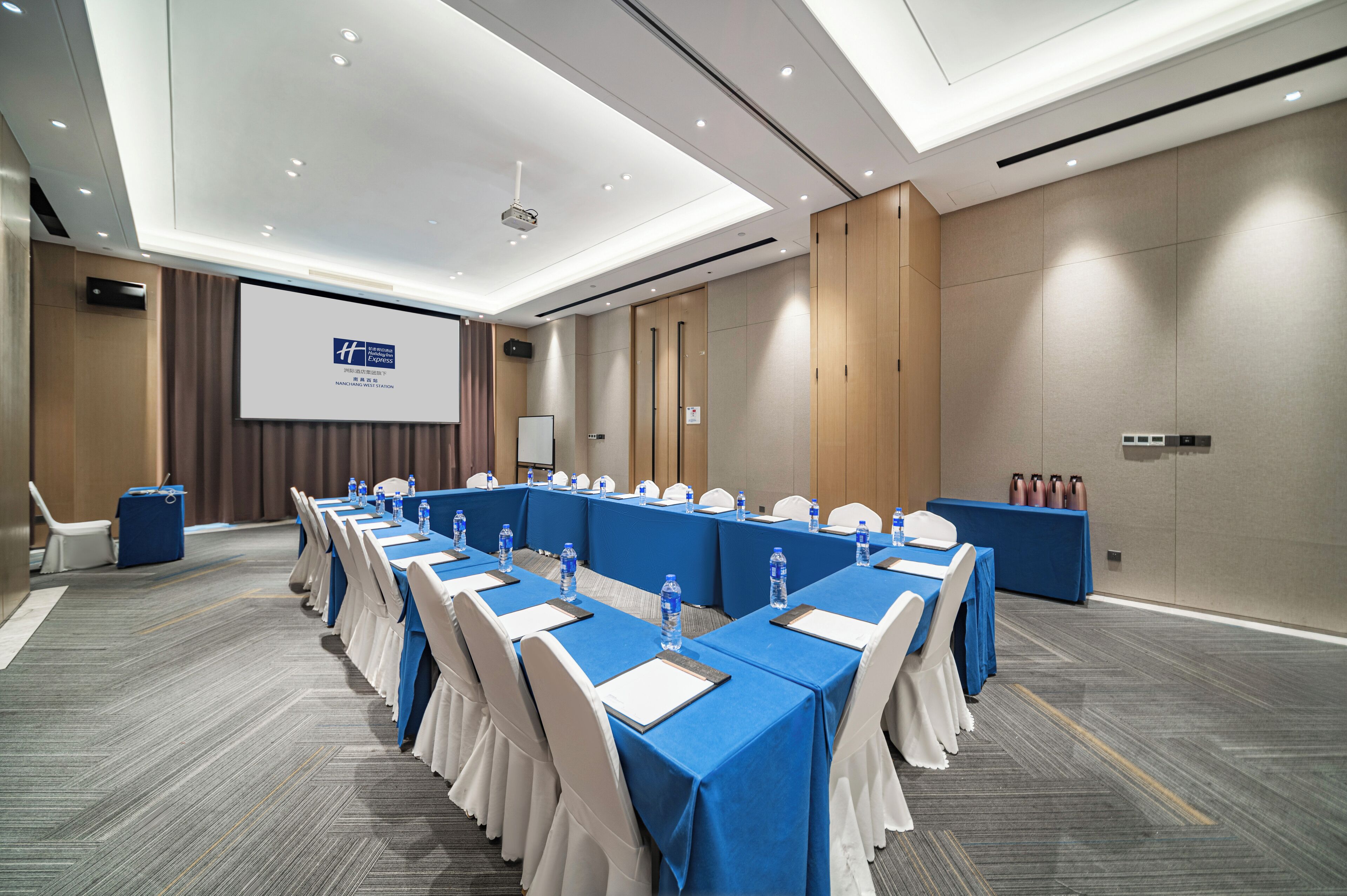 Uma sala de conferências com uma mesa comprida, cadeiras e tela de projeção.