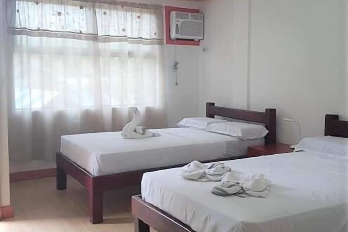 Quarto de hotel com duas camas de solteiro, uma janela com cortinas leves e uma luminária no teto.