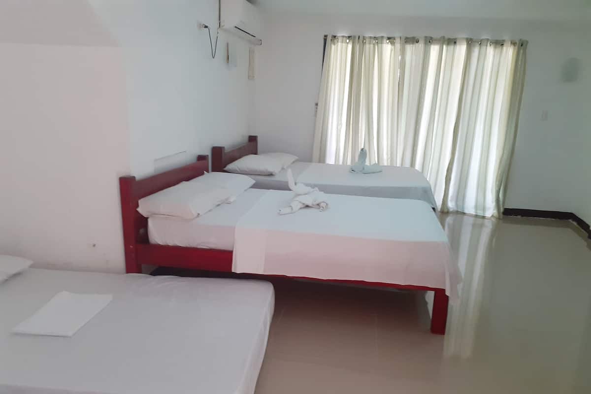 Quarto de hotel com duas camas de solteiro, cabeceira de madeira, cortina branca e chão de azulejos.