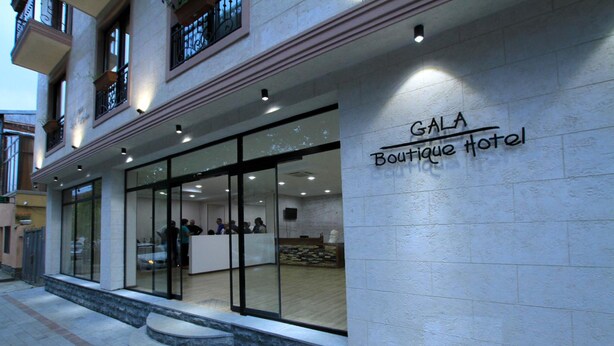 Exterior do Gala Boutique Hotel, com uma área de recepção visível através das portas de vidro.
