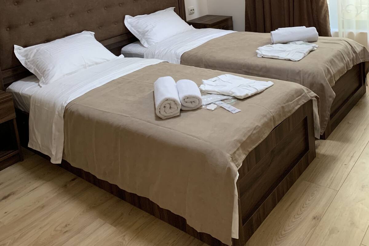 Quarto de hotel com duas camas, cada uma com cabeceira, roupa de cama branca e toalhas.