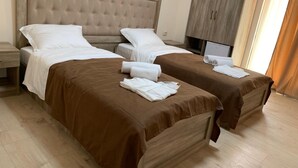 Quarto de hotel com duas camas, cabeceira de madeira, guarda-roupa e televisão.