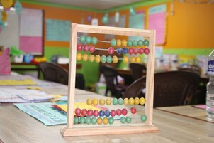 Um ábaco de madeira com contas coloridas sobre uma mesa em uma sala de aula.