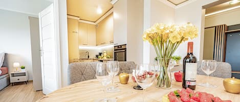 Uma mesa de jantar posta com taças de vinho, uma garrafa de vinho e um prato de morangos em uma cozinha moderna com um sofá e um espaço para refeições.