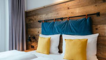Quarto de hotel com cabeceira de madeira, duas camas com roupa de cama branca e amarela, e uma janela com cortinas.