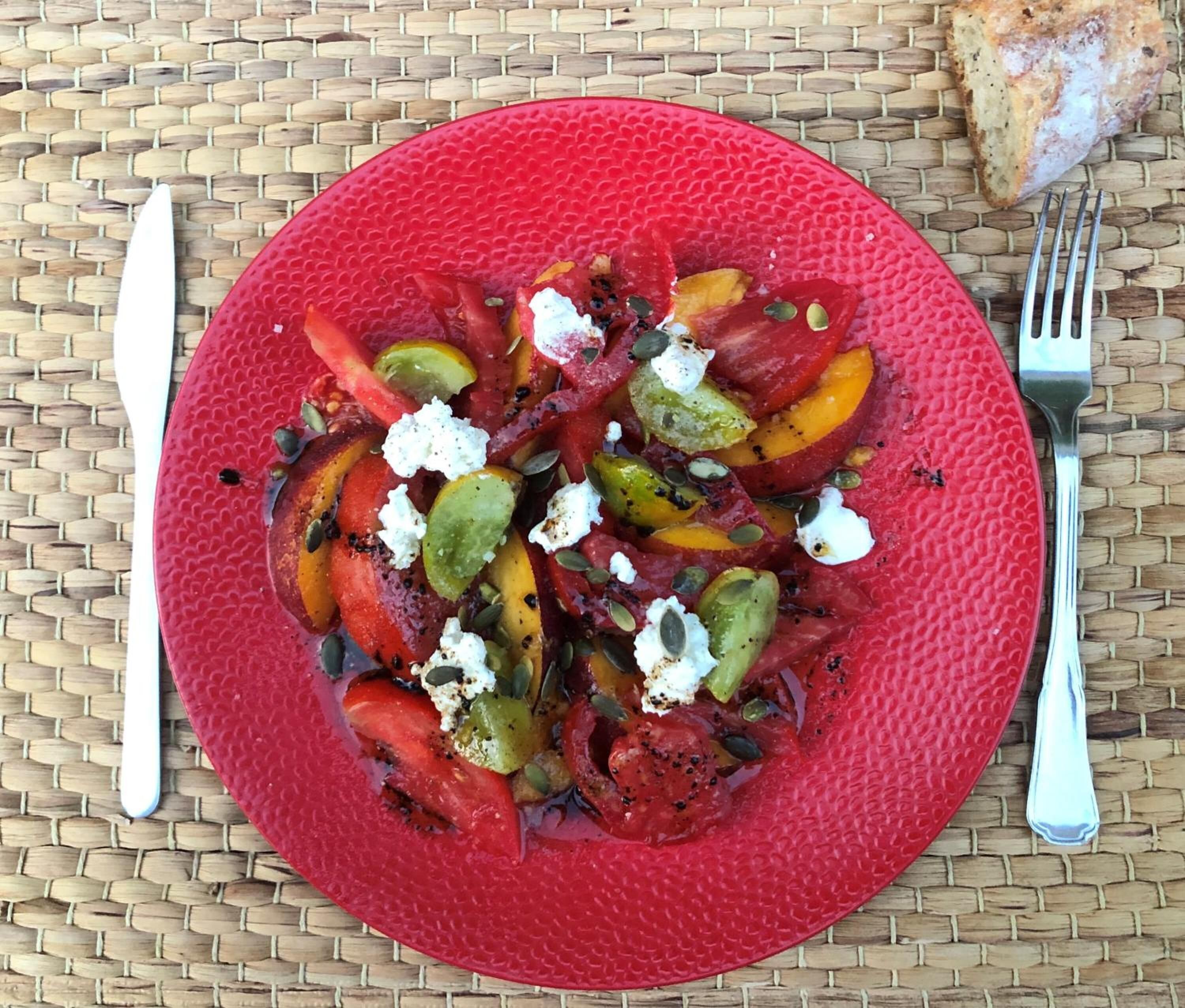 Um prato vermelho com salada sobre uma toalha de mesa trançada.