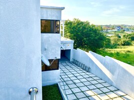 Um edifício moderno com fachada branca, uma pequena varanda com chão de azulejos e vista para uma paisagem verde.