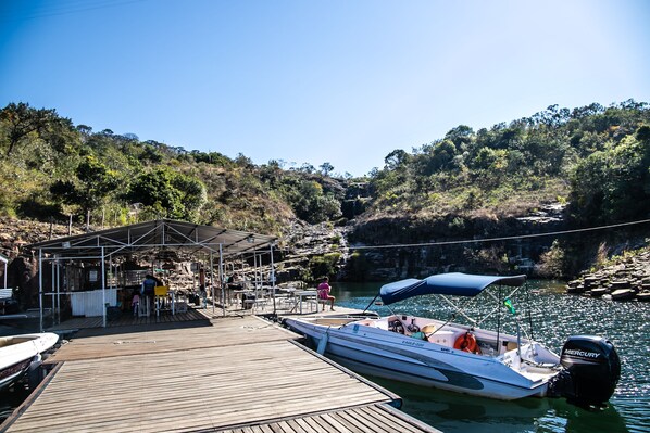 Um cais de madeira com área de estar coberta, um barco e um morro rochoso ao fundo.