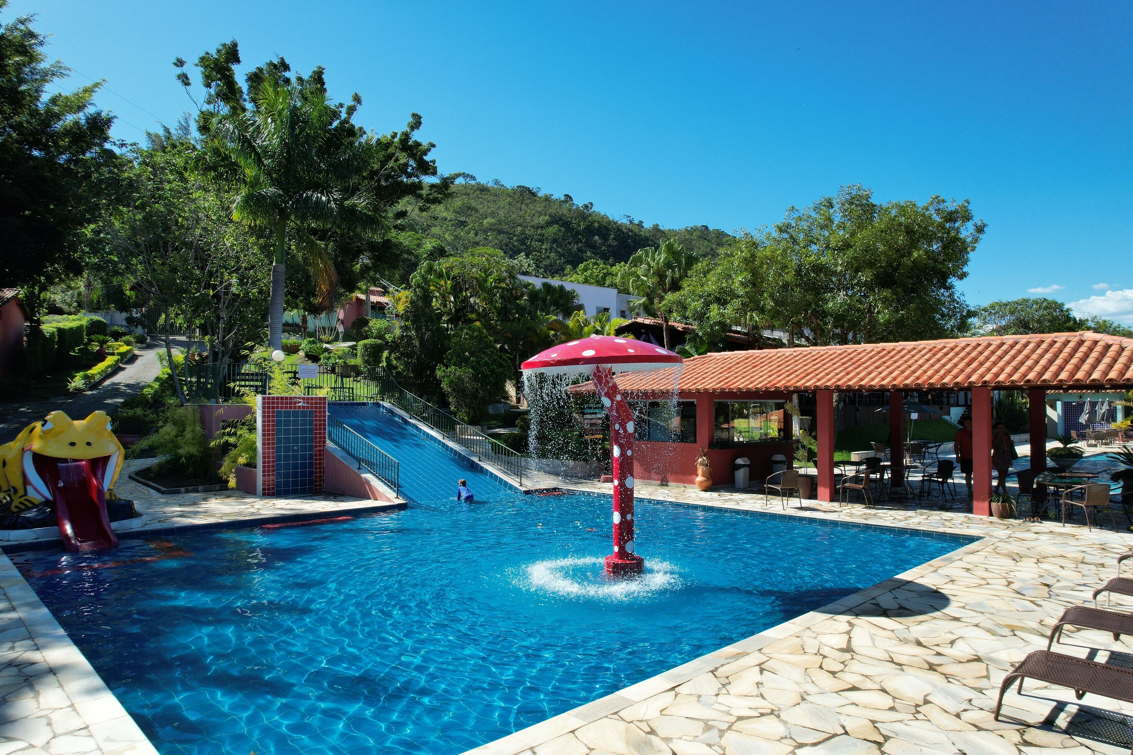 Uma piscina com fonte de água, rodeada por azulejos de pedra e vegetação.