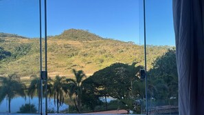 Vista pela janela com montanha ao fundo, palmeiras e um corpo de água.