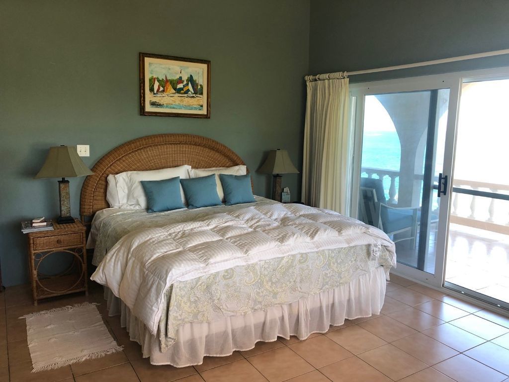 Quarto com uma cama grande, duas mesas de cabeceira, um quadro na parede e uma porta de vidro deslizante para uma varanda.