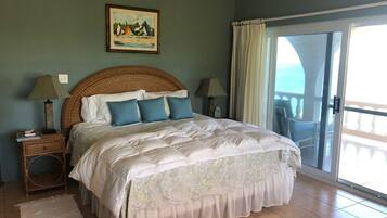 Quarto com uma cama grande, duas mesas de cabeceira, um quadro na parede e uma porta de vidro deslizante para uma varanda.