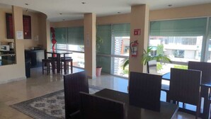 Um hall de hotel com balcão de recepção, área de estar e grandes janelas com vista para a rua.