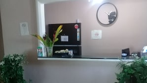 Uma mesa de recepção com um relógio, um mural de avisos e plantas em vasos.