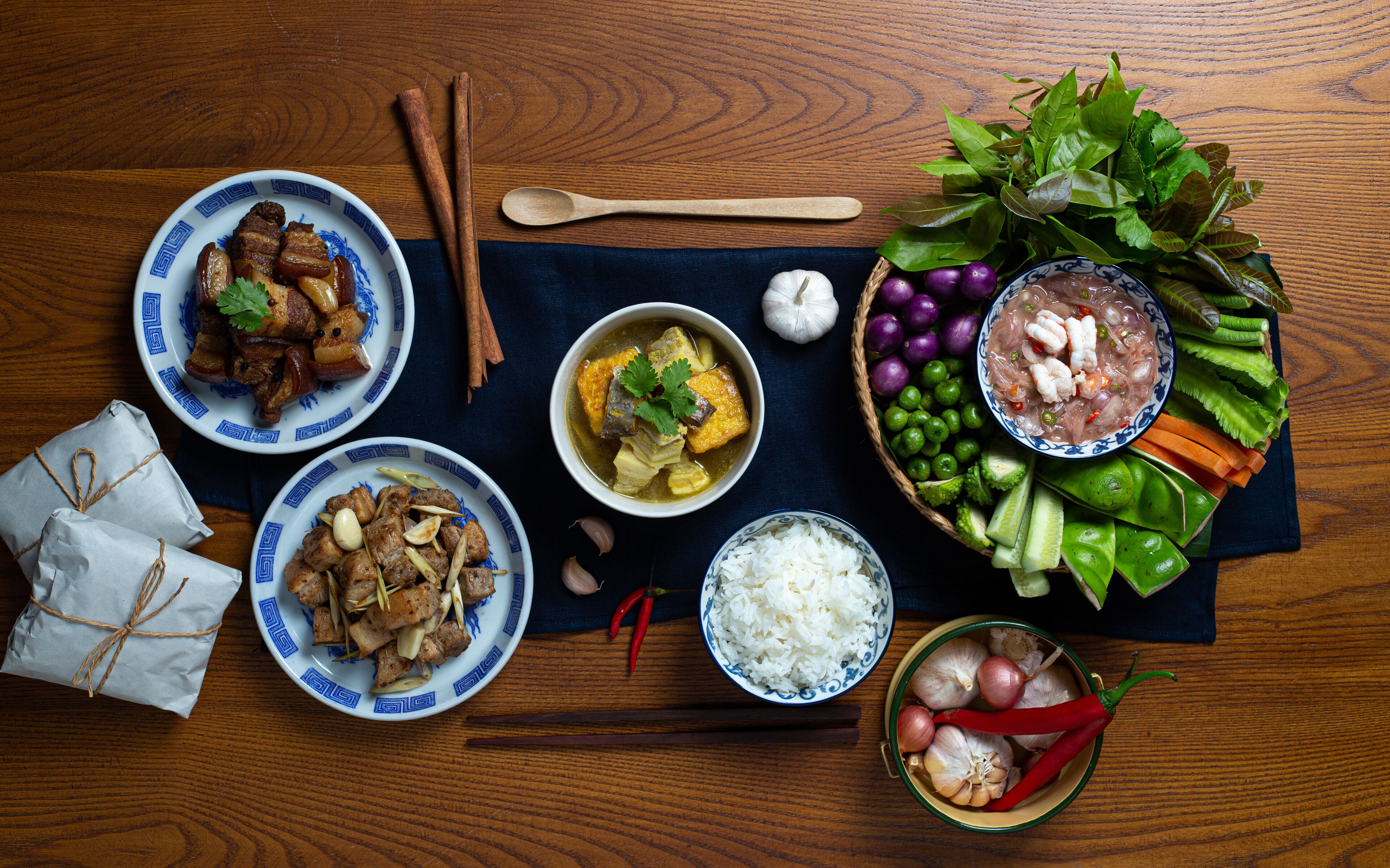 Uma mesa de madeira com vários pratos, incluindo carne, legumes e arroz, dispostos de forma organizada.