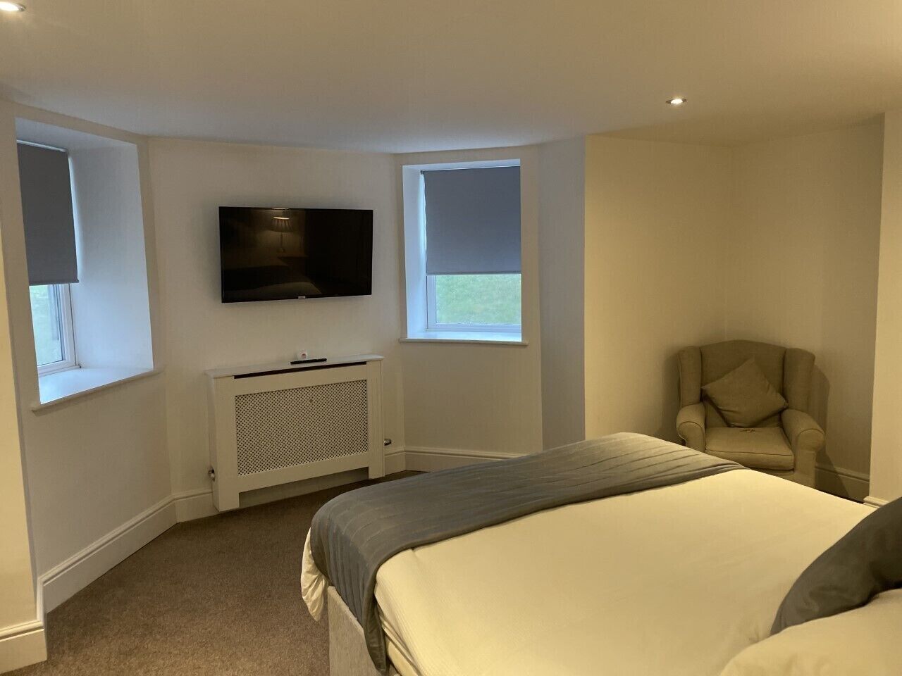 Quarto com cama, cadeira, televisão e radiador.