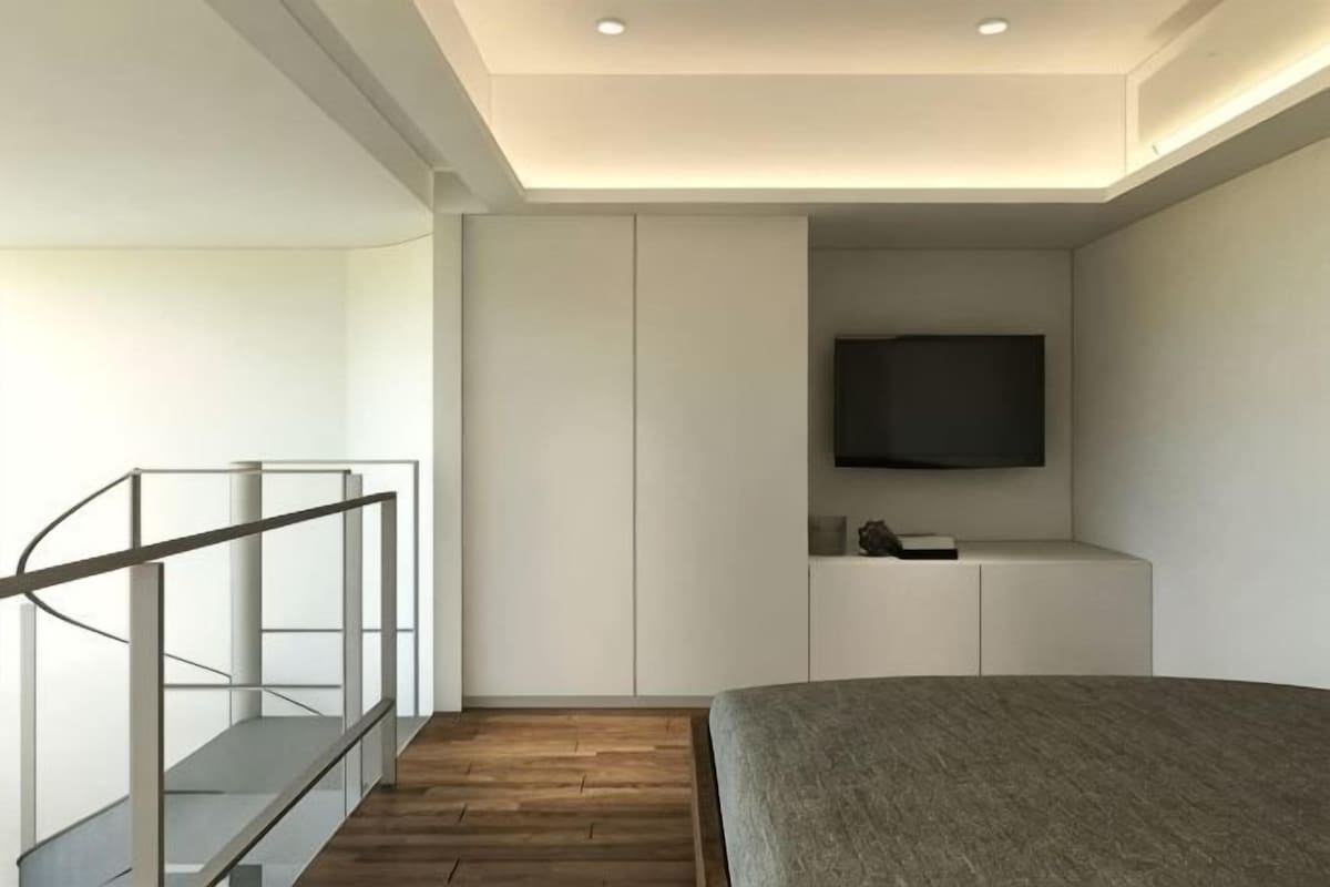 Quarto moderno com cama, TV fixada na parede e escada com guarda-corpo de vidro.