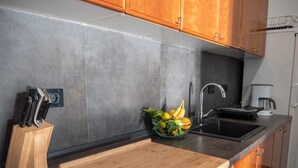 Uma cozinha moderna com azulejos cinza, armários de madeira, uma pia, tábua de corte e uma tigela de frutas.