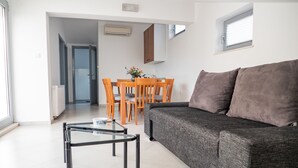 Uma sala de estar moderna com um sofá cinzento, uma mesa de centro de vidro e uma área de jantar com cadeiras e mesa de madeira.